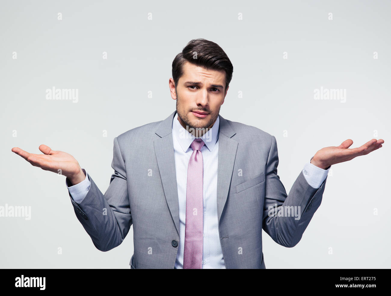 Businessman shrugging shoulders over gray background. Looking at camera ...