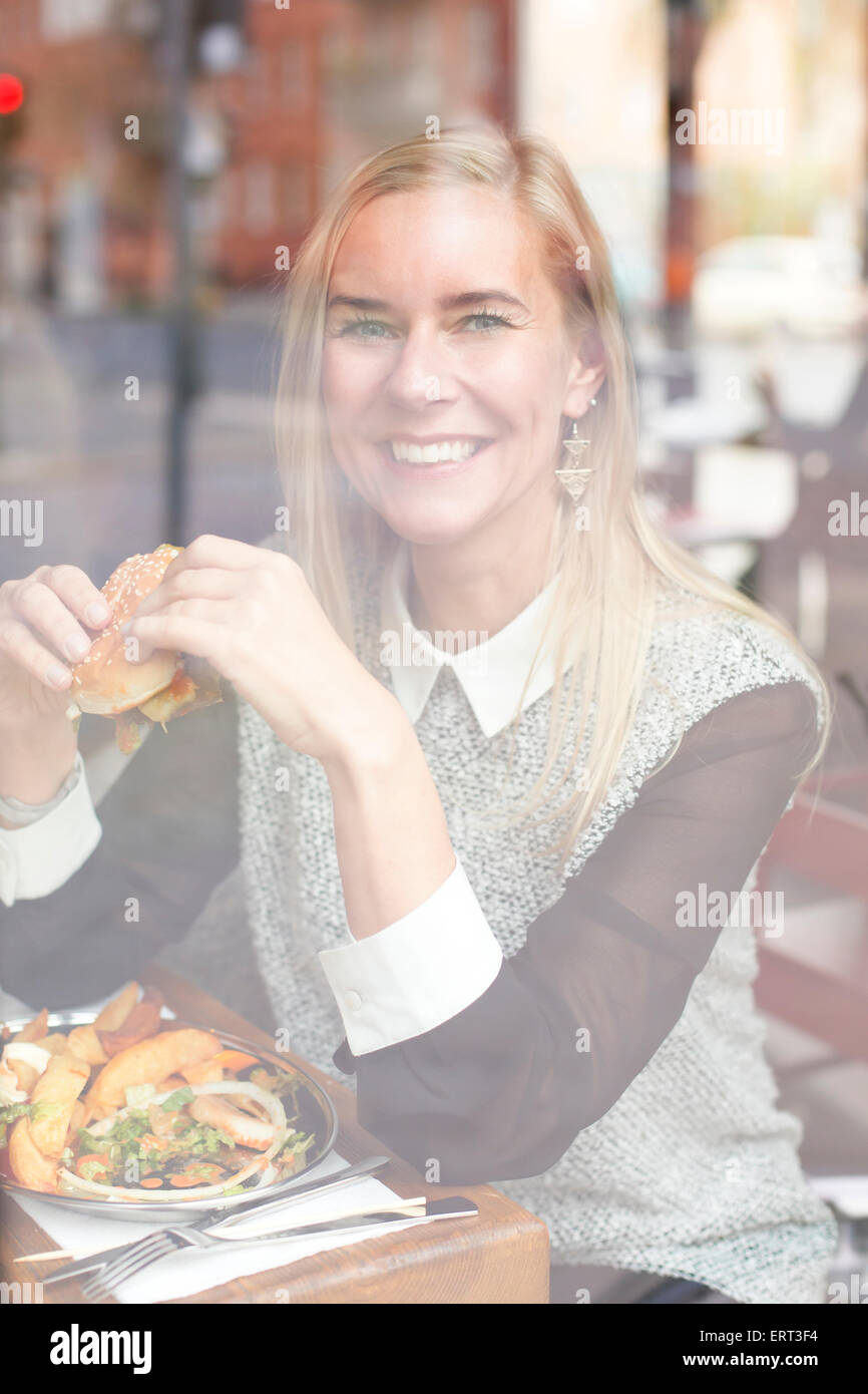 blond woman eating a burger and looking through window Stock Photo - Alamy