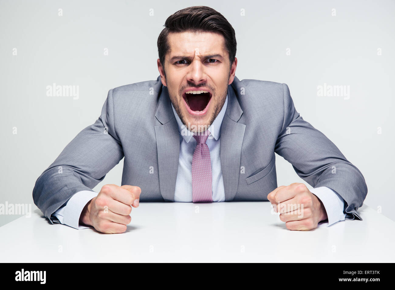 Angry businessman sitting at the table and shouting over gray ...