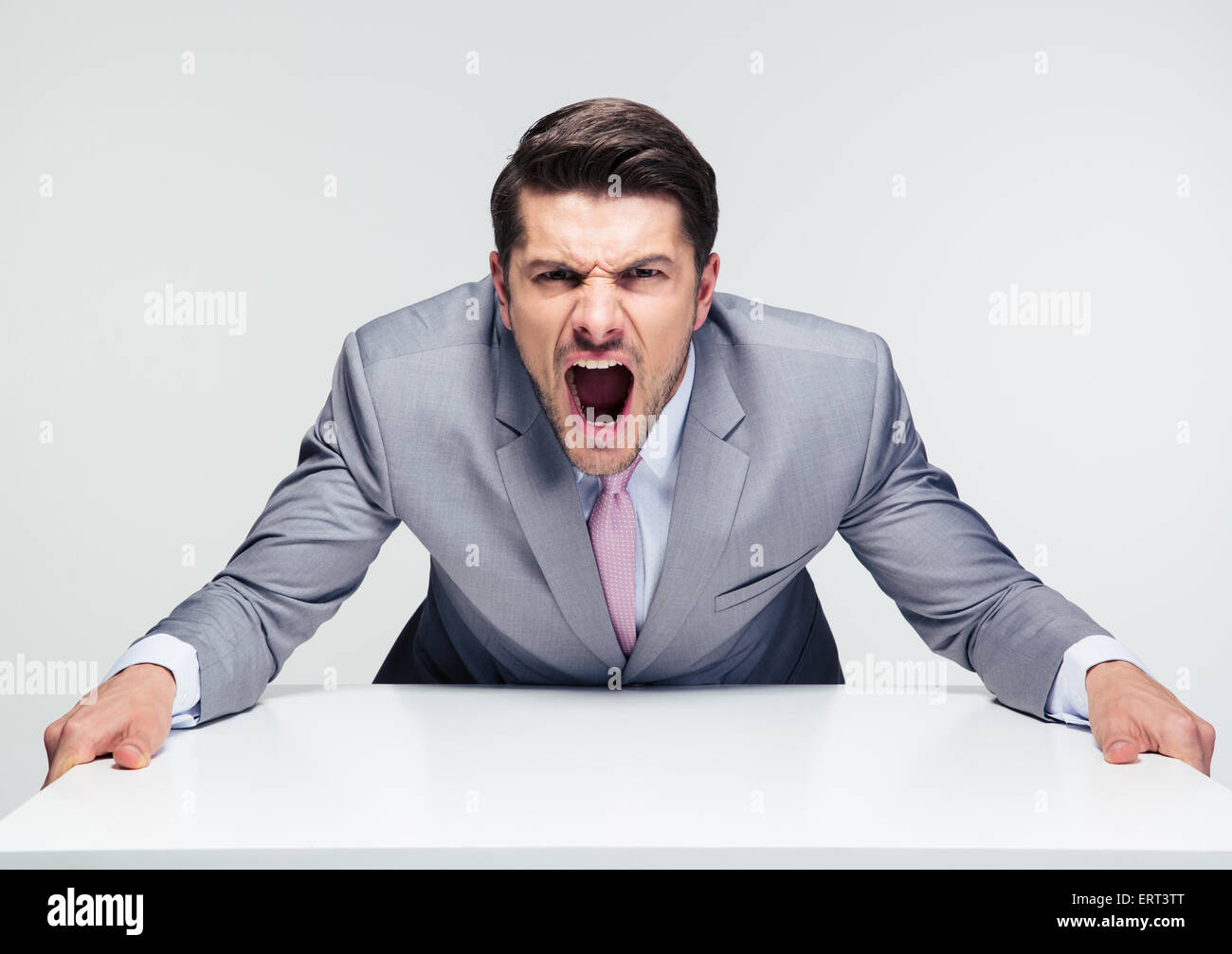 Angry businessman sitting at the table and screaming over gray ...