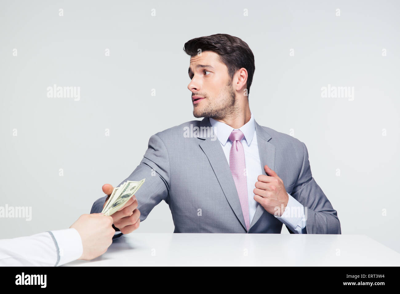 Businessman sitting at the table and taking bribe over gray background ...