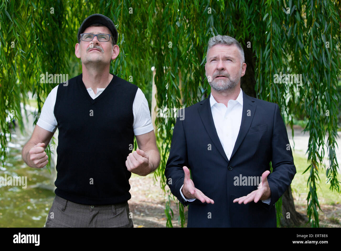 two businessmen standing together in a park and looking annoyed to the ...