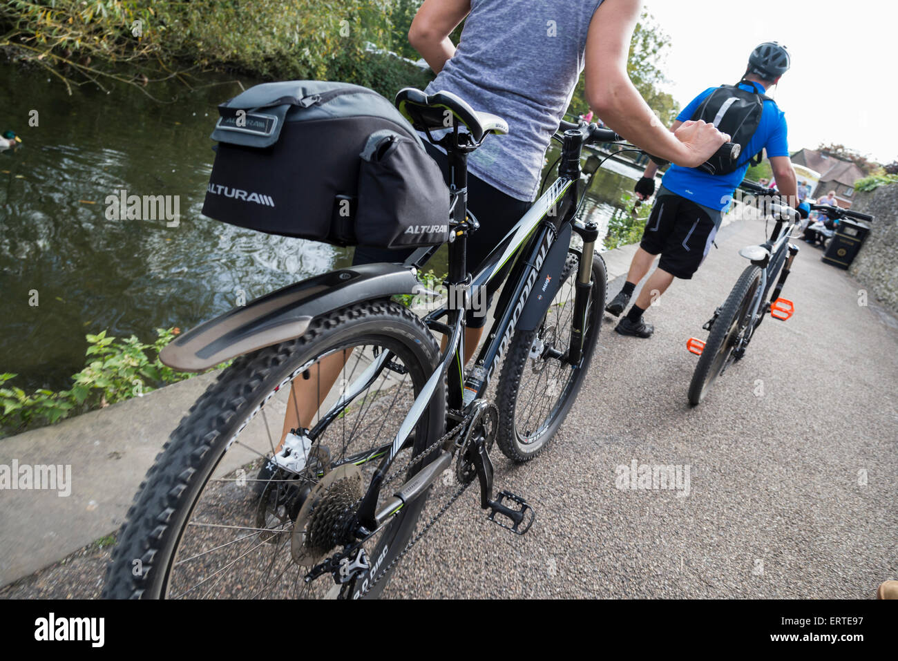 Back wheel and back of person walking along footpath pushing bicycle ...