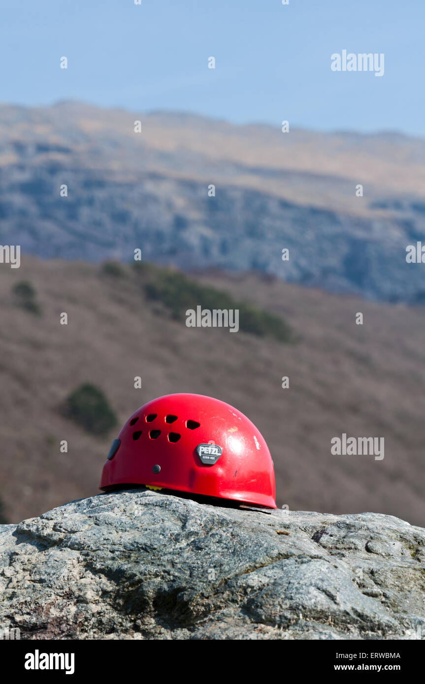 Sunlight highlights a red climber's safety helmet put aside on a rock ...
