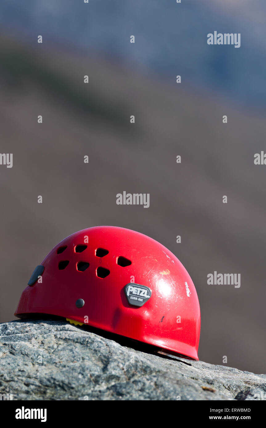 Sunlight highlights a red climber's safety helmet put aside on a rock ...