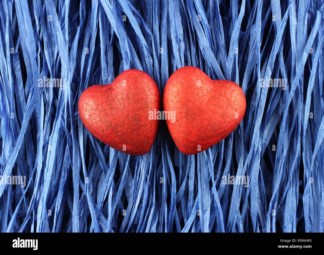 Two red painted polyfoam hearts on blue paper raffia strips background ...