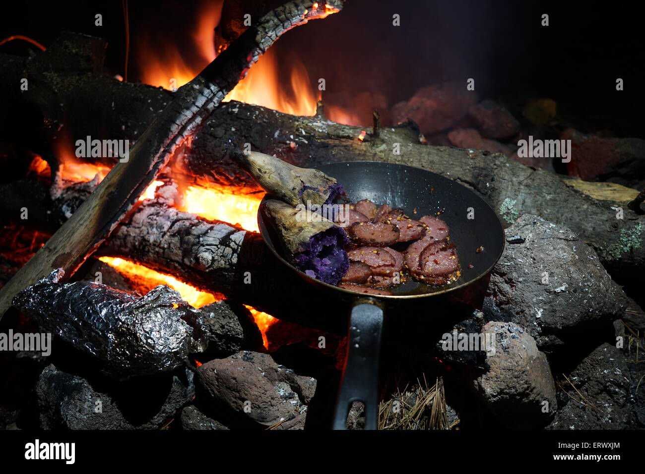 Cooking salami and purple sweet potato in pan over camp fire Stock ...