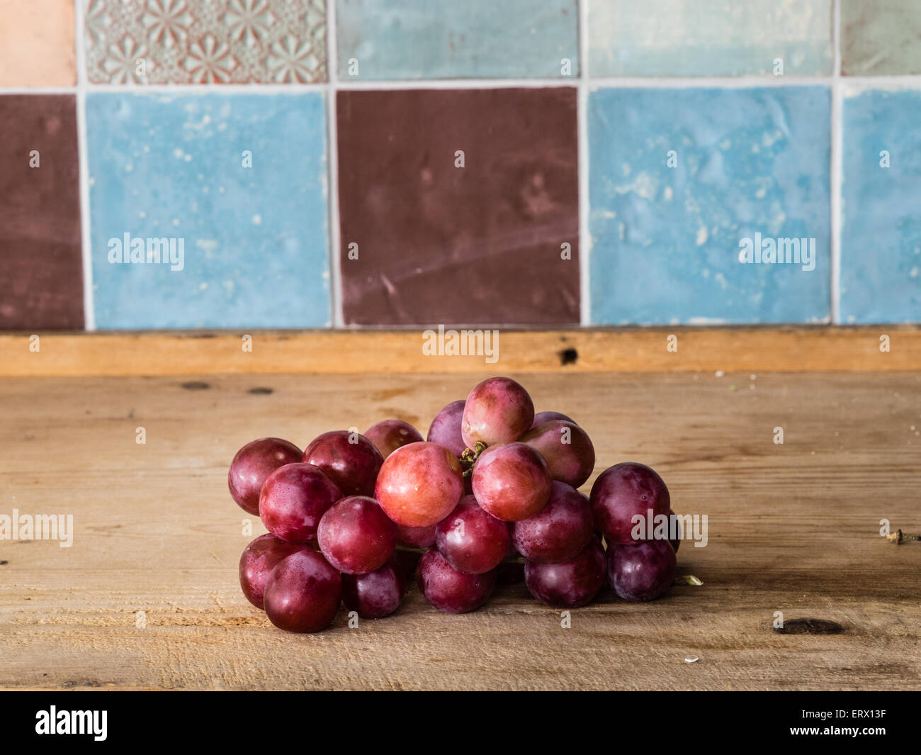 Harvested red grapes in a kitchen table in front of colorful tiles ...