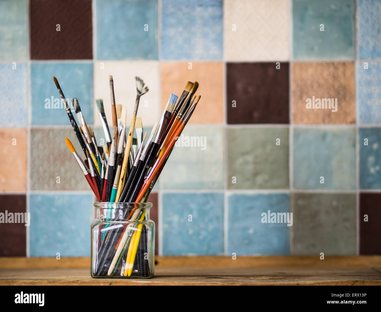 Bunch of paint brushes in a glass jar in front of a colorful tiled wall ...