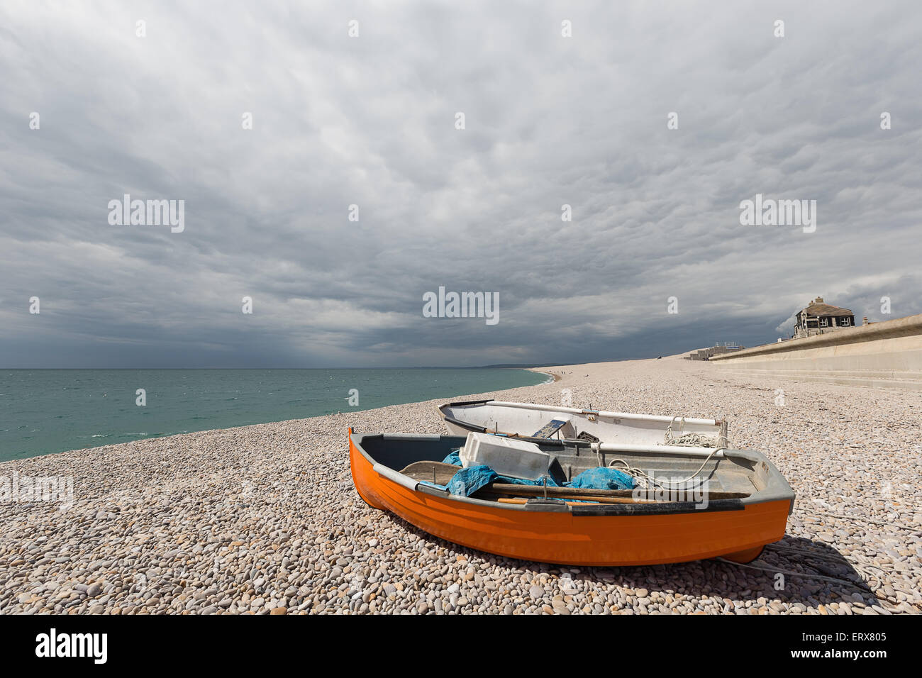 Two small boats lying on shingle beach in bright sunshine with looming ...