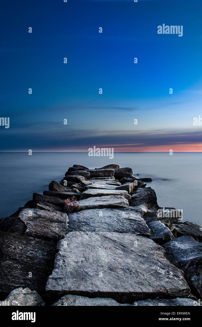 Rock pier looking out to an inviting morning sunrise Stock Photo - Alamy