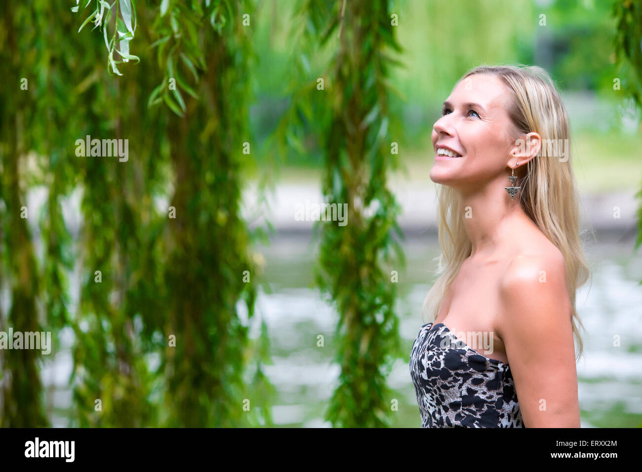 blond woman standing by a river besides a tree Stock Photo - Alamy