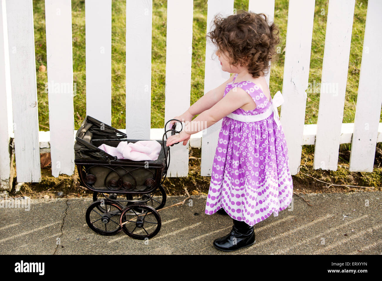 little girl pushing a vintage stroller in front of a white fence Stock ...