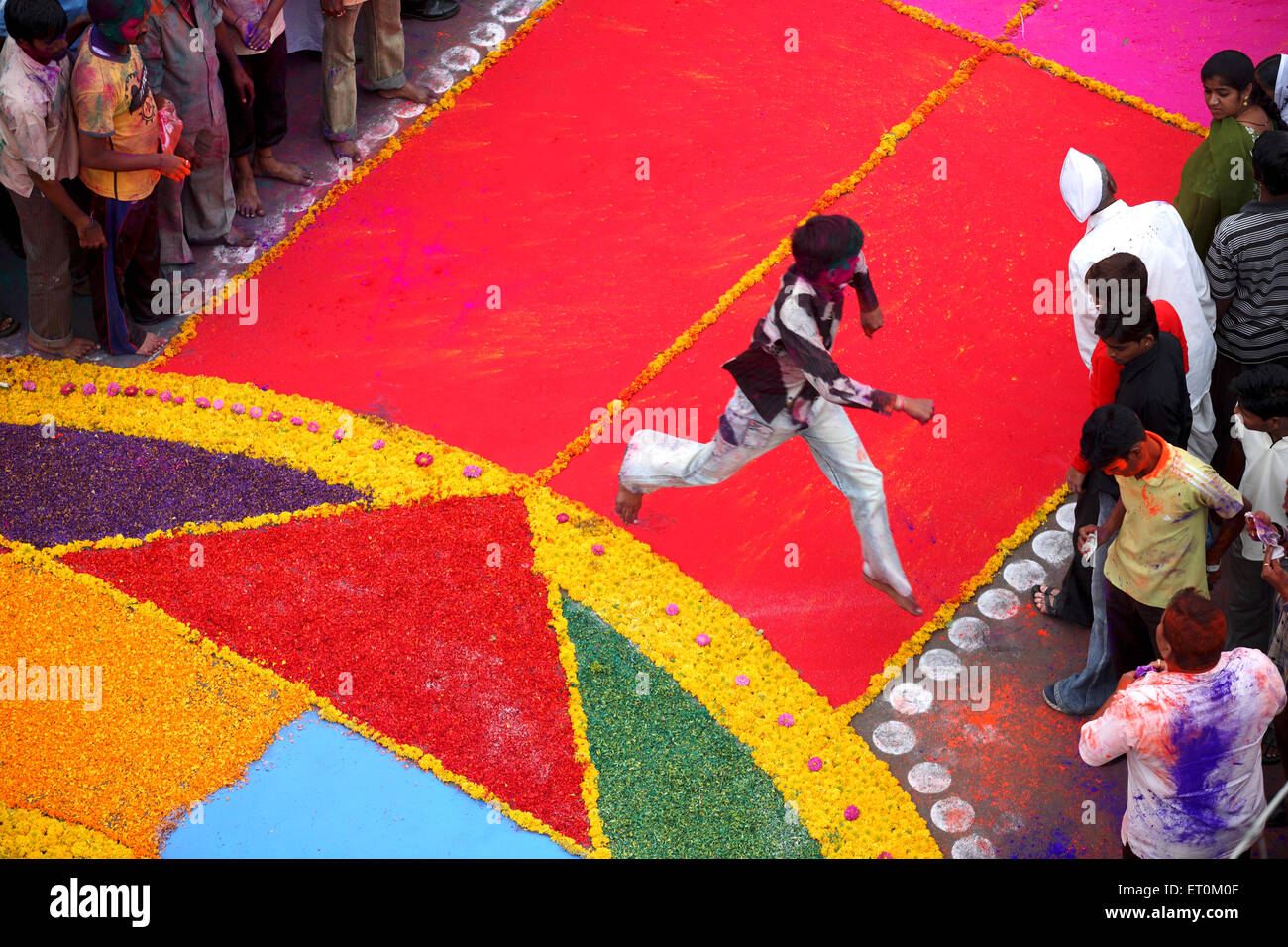 Boy taking leap near colourful flower Rangoli made on road for ...