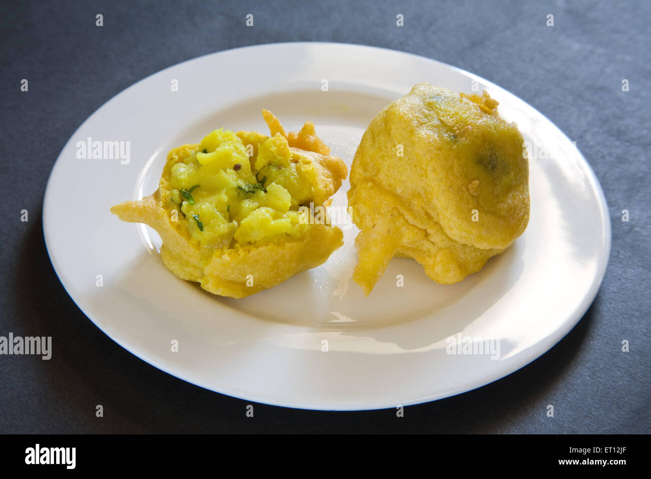 Indian fast food fried batata potato vada served in plate on black ...