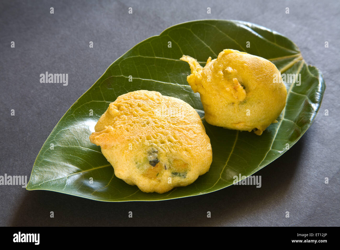 Indian fast food fried batata potato vada served in leaf on black ...