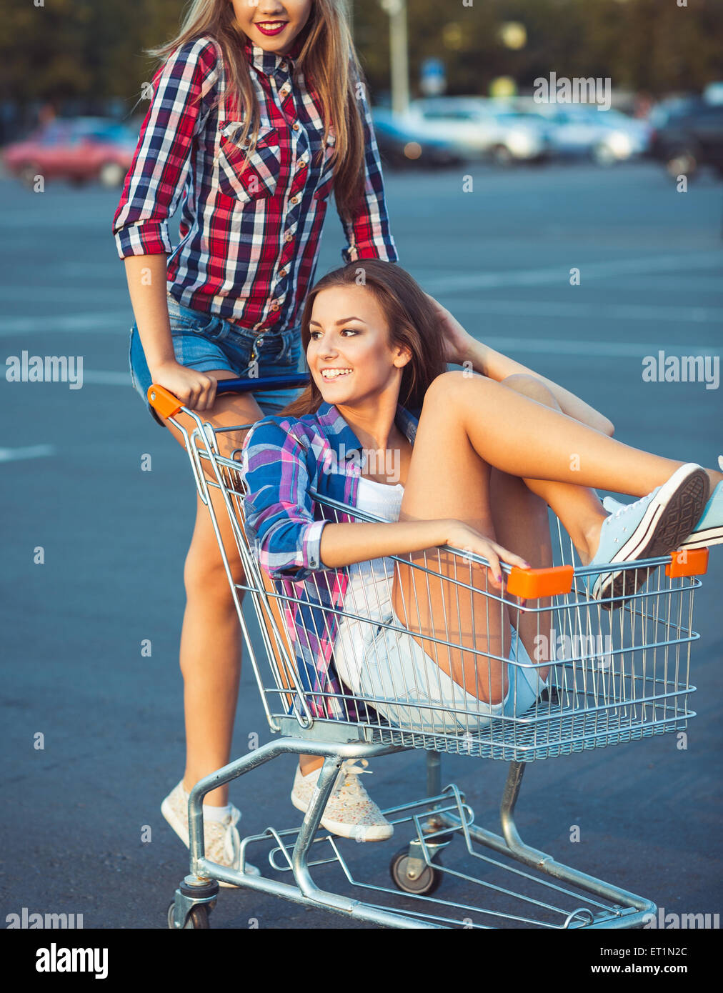 Two happy beautiful teen girls driving shopping cart outdoors ...