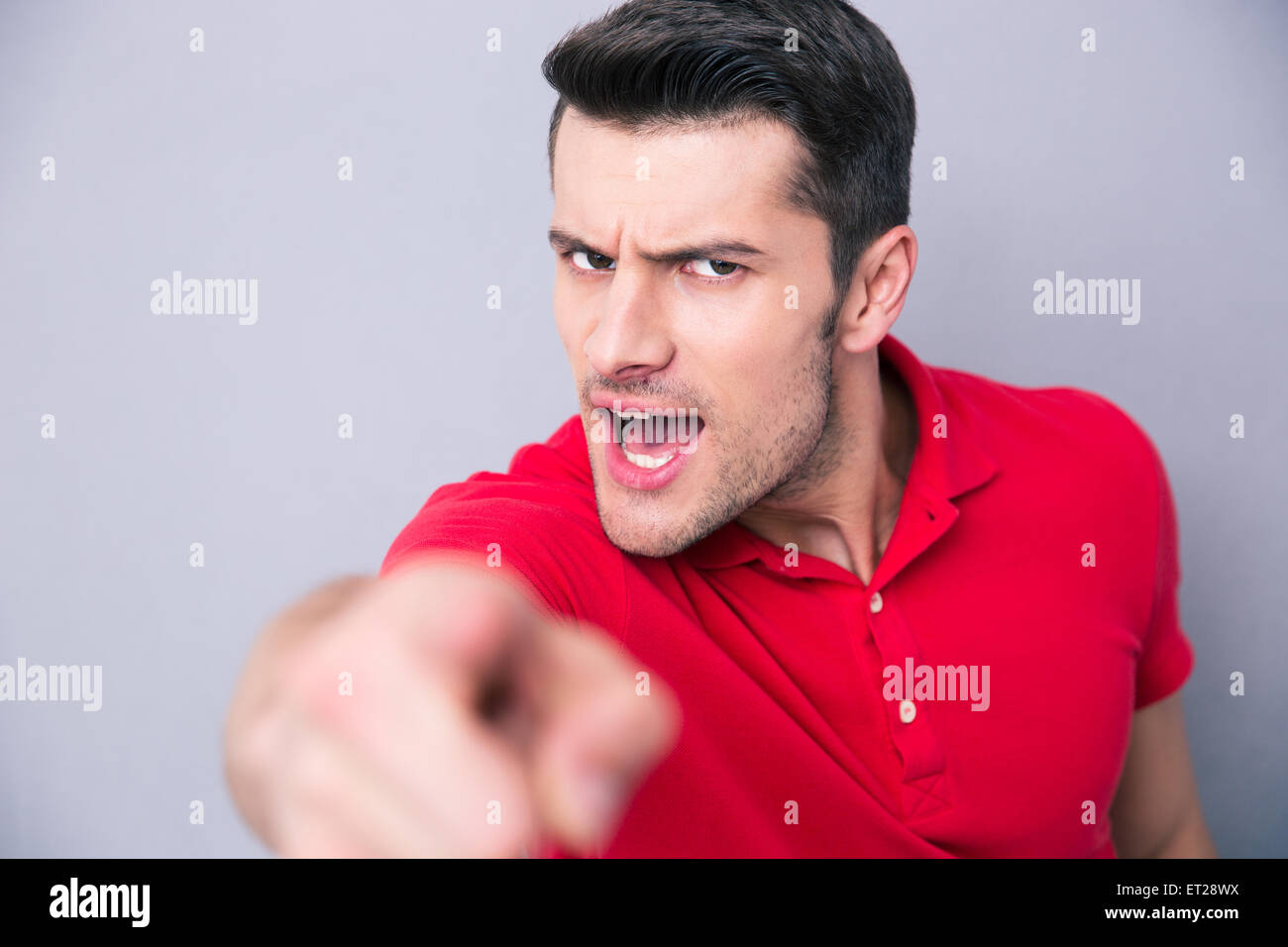 Casual man shouting and pointing finger at camera over gray background ...