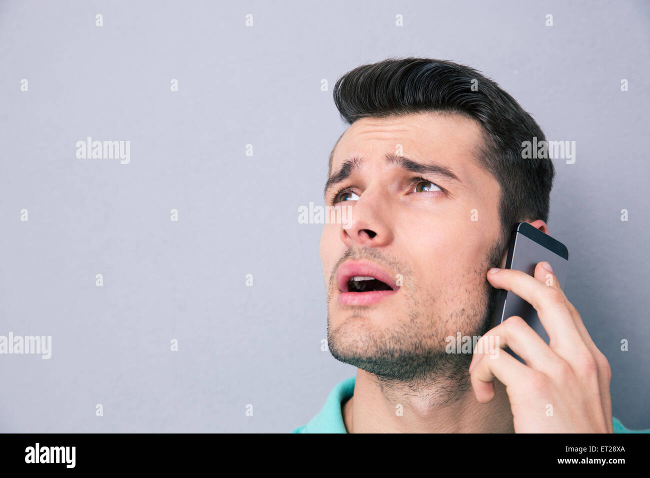 Closeup portrait of a pensive young man talking on the phone over gray ...