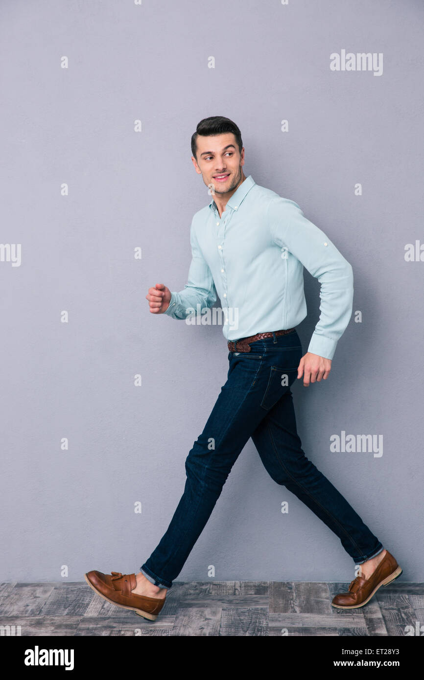 Happy young man walking over gray background and looking away Stock ...