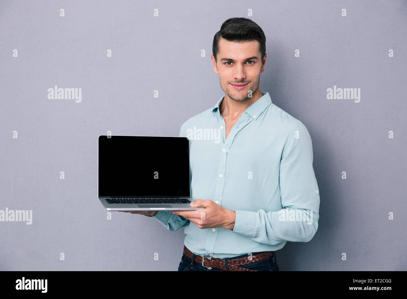 Handsome casual man showing blank laptop screen over gray background ...