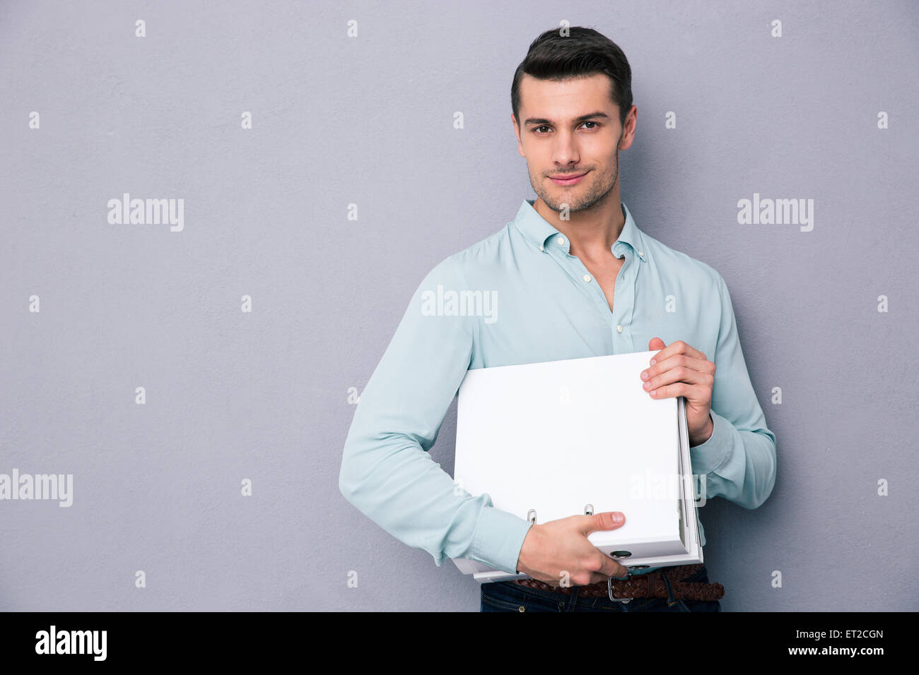 Handsome young man holding folders over gray background. Looking at ...