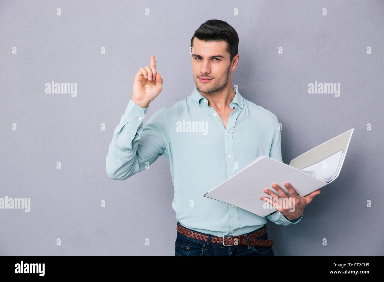 Handsome man holding folder and pointing finger up over gray background ...