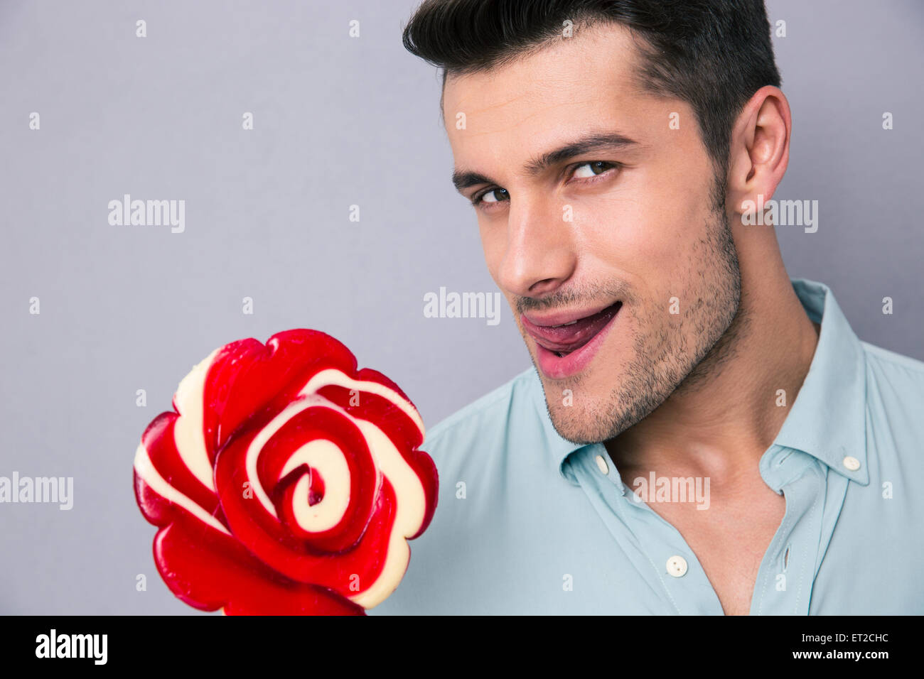 Portrait of a young man holding lollipop over gray background. looking ...