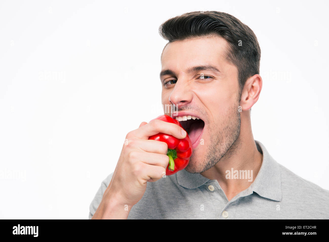 Young man biting pepper isolated on a white background. Looking at ...