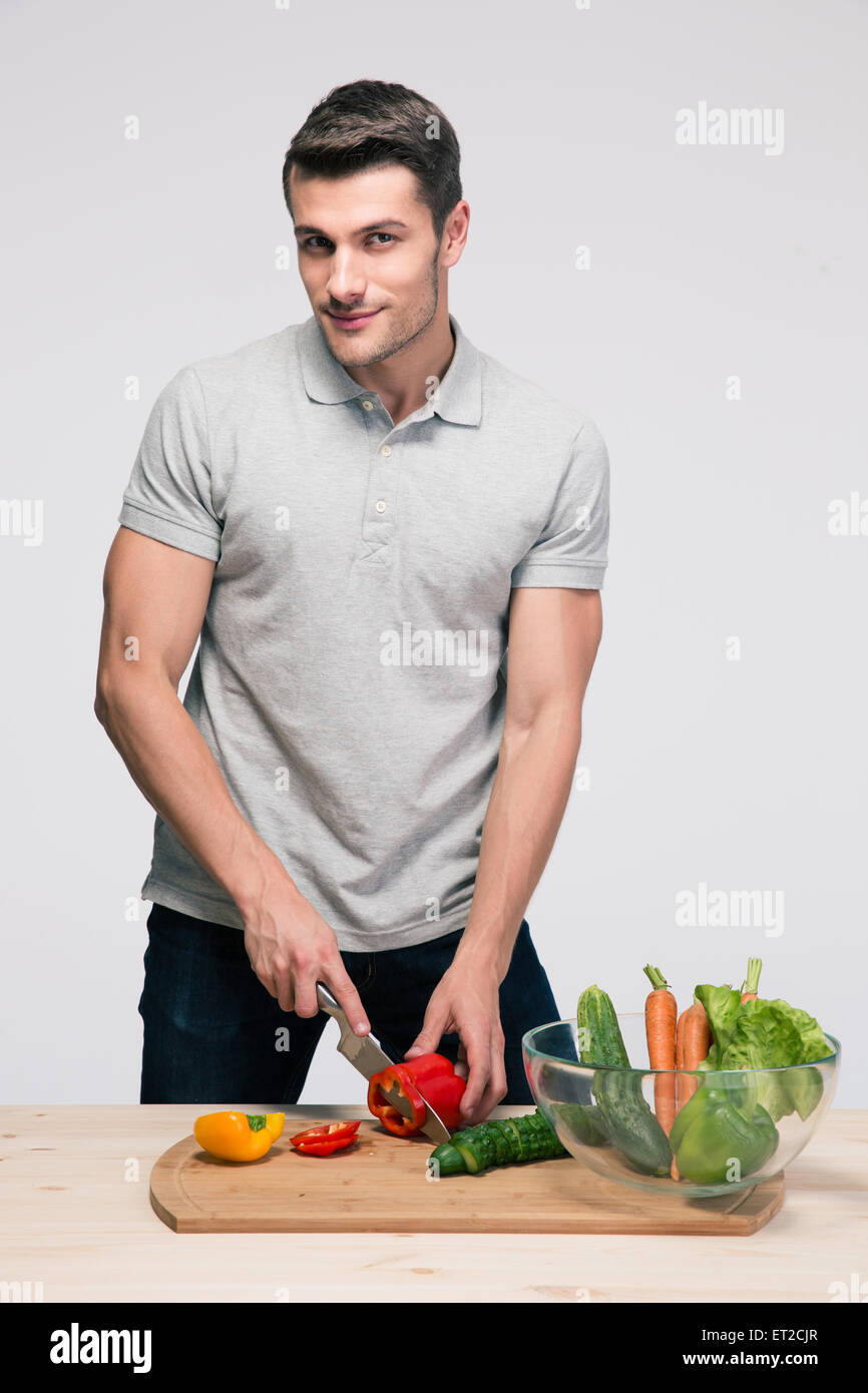 Happy young man cutting vegetables over gray background. Looking at ...