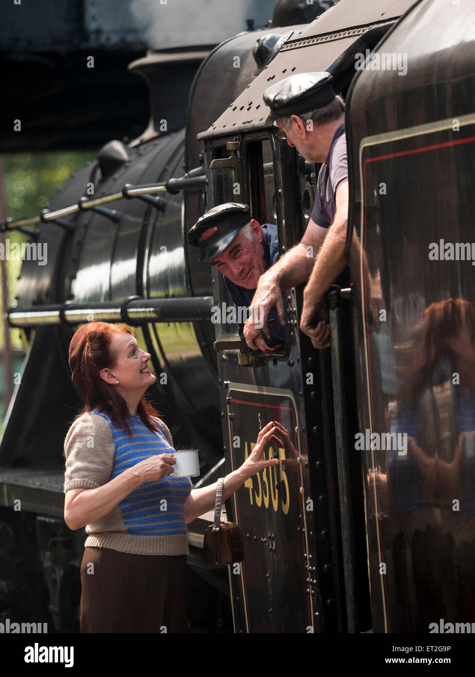 engine driver of a vintage steam locomotive talks to a lady in WW2 era ...