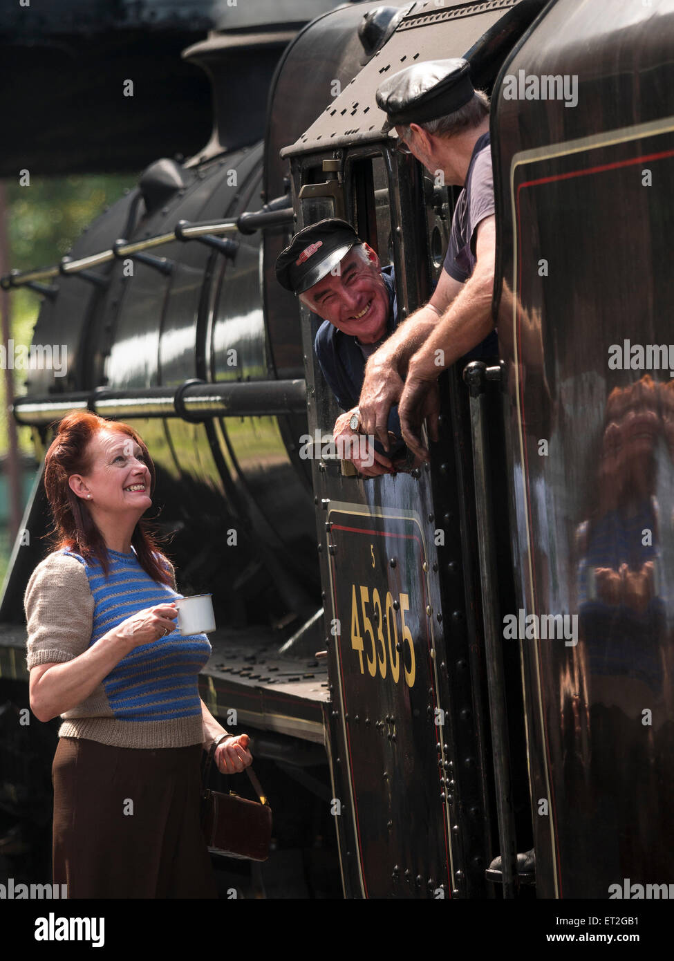 engine driver of a vintage steam locomotive talks to a lady in WW2 era ...