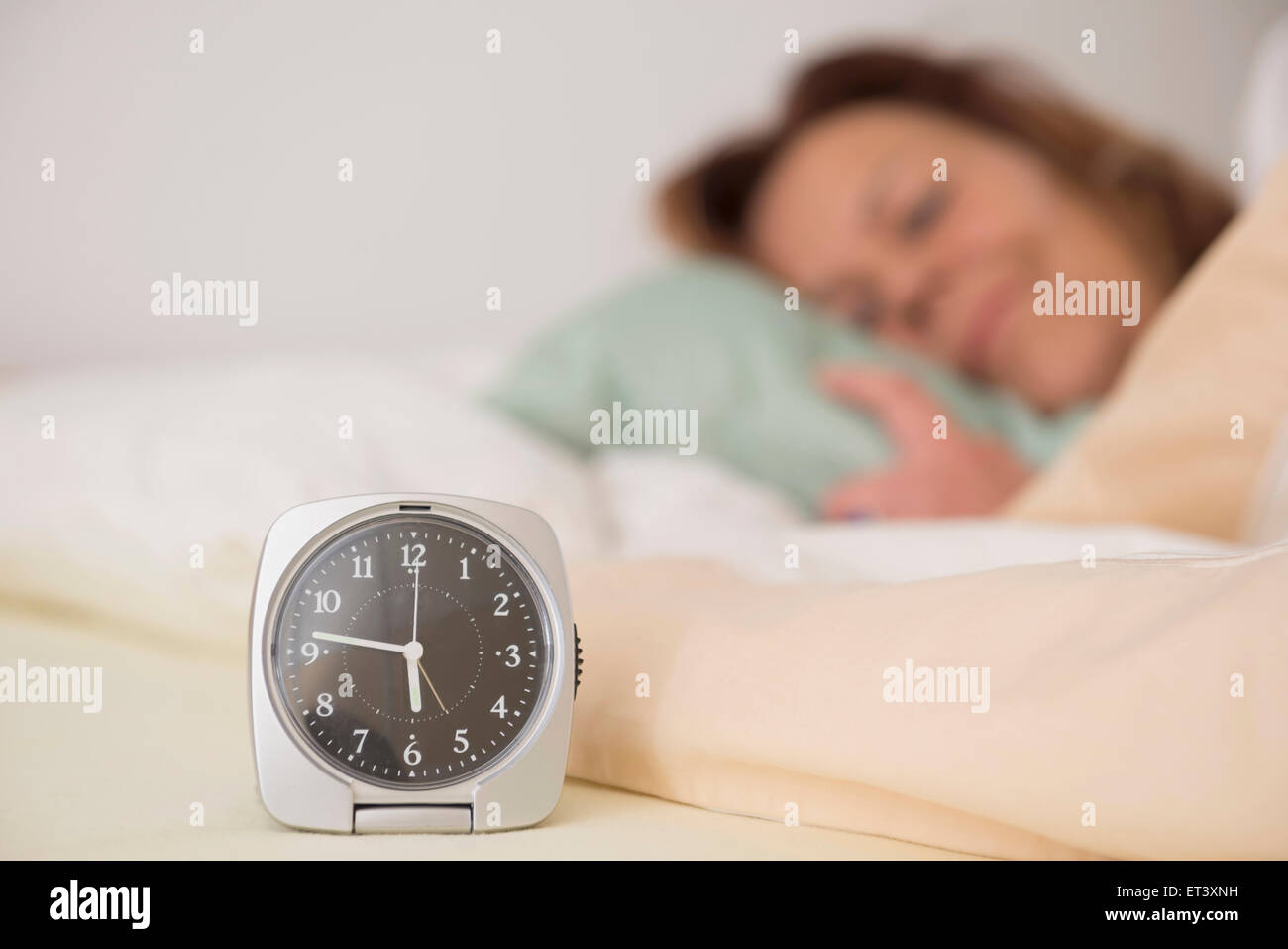 Woman asleep in bed while her alarm shows the early time at home in ...