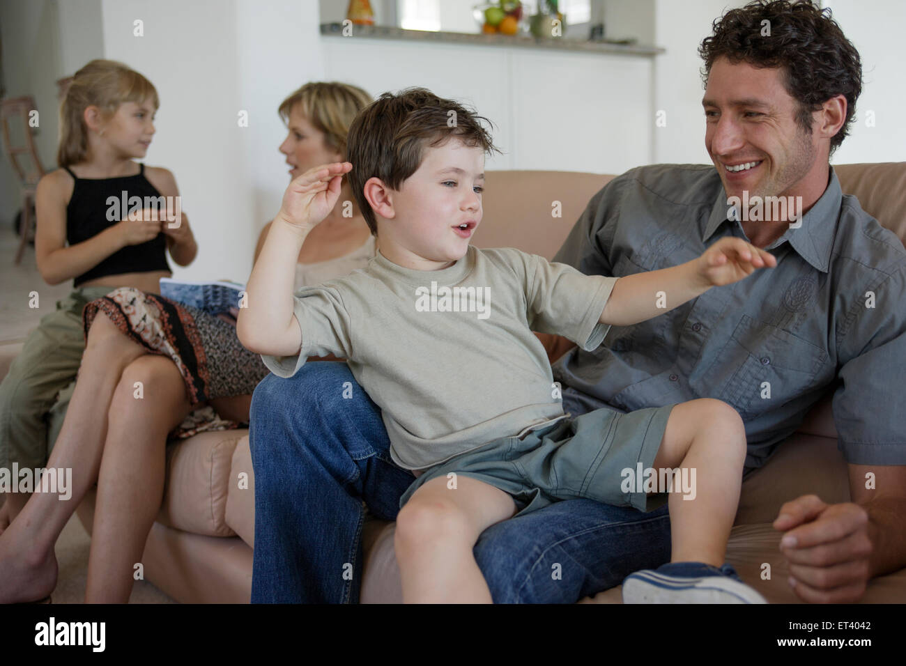 Family with two kids on a couch, son on fathers lap, gesturing Stock ...