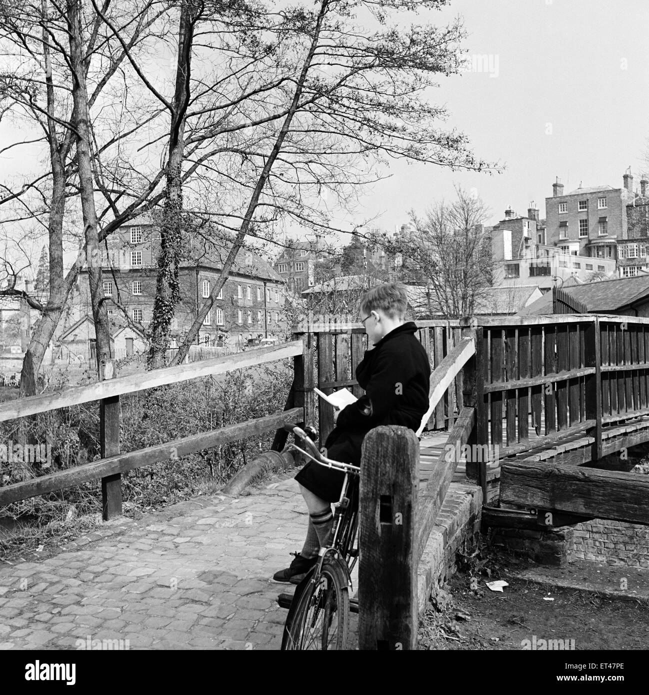 A boy reading a book by a bridge crossing the River Wey, in Guildford ...