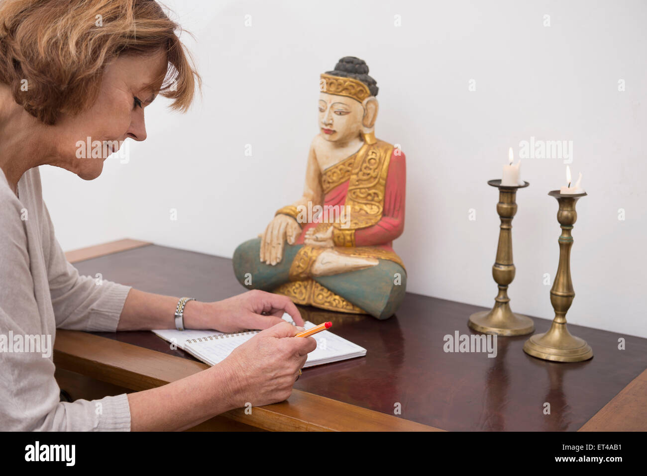 Senior woman writing in notebook, Buddha statue and candles in the ...