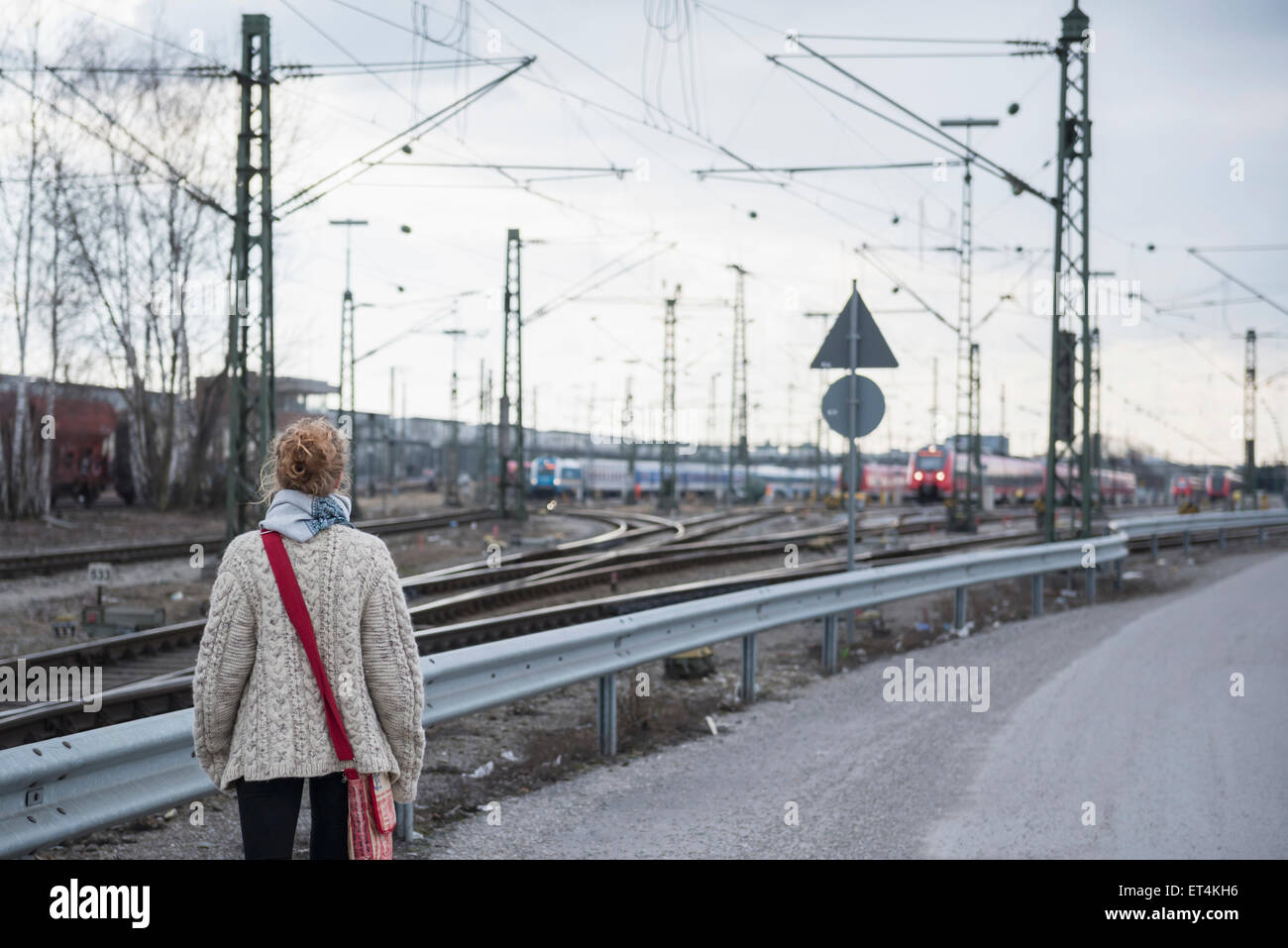 Rear view of a young woman curiously looking at train on railway track ...