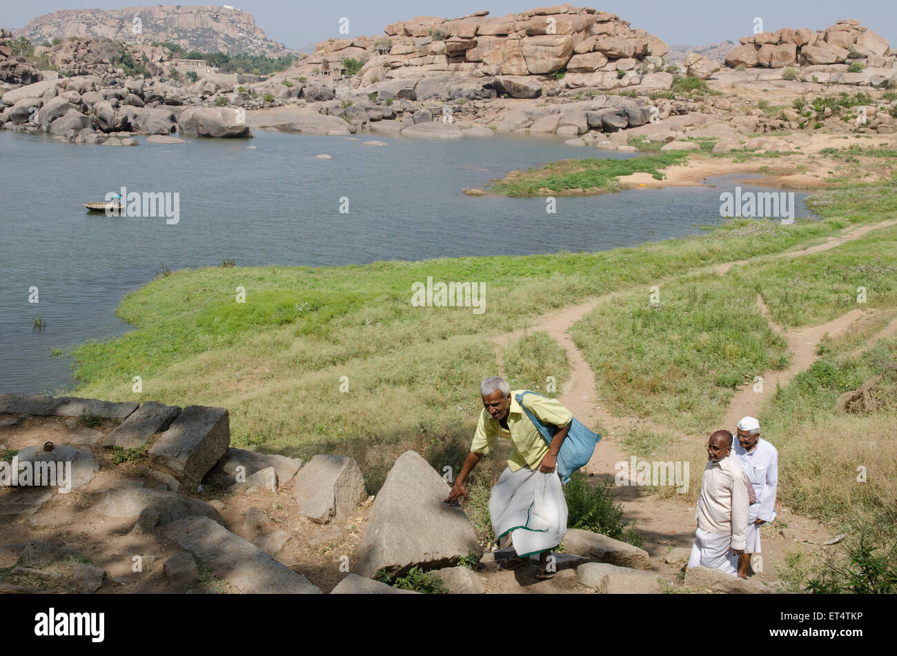 three men walk accross the landscape at the ancient city of Hampi ...