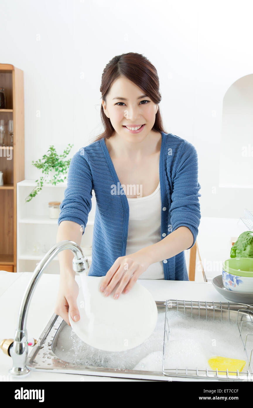 Young woman washing plates and smiling at the camera Stock Photo - Alamy
