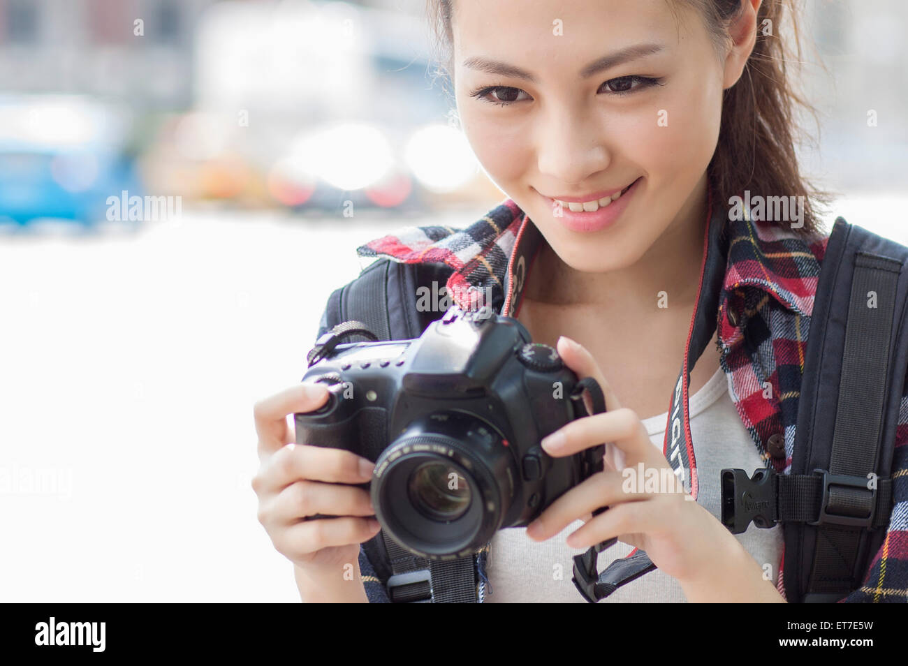 Young woman holding camera and looking down with smile Stock Photo - Alamy