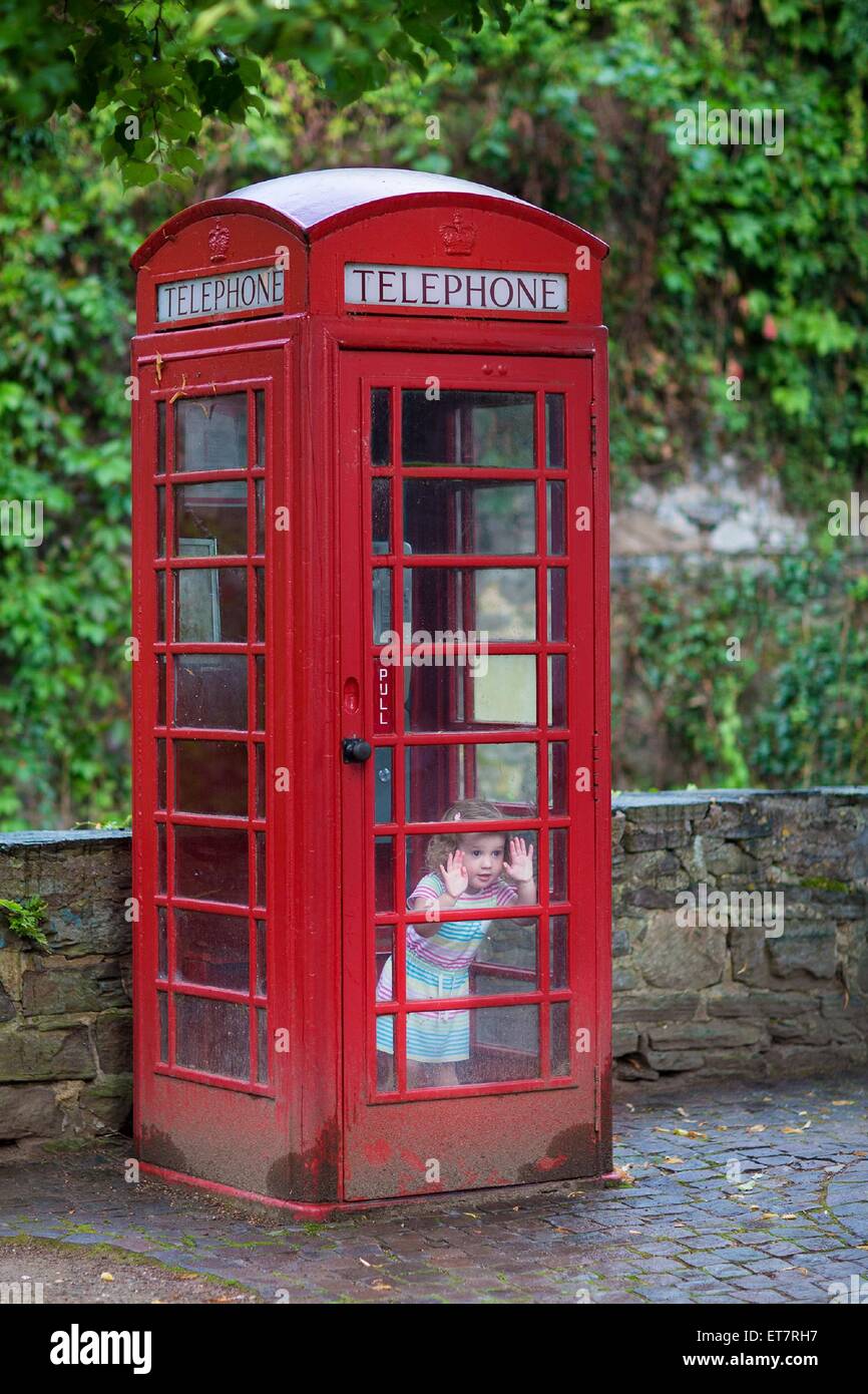 Funny little girl hiding and playing in a traditional English telephone ...