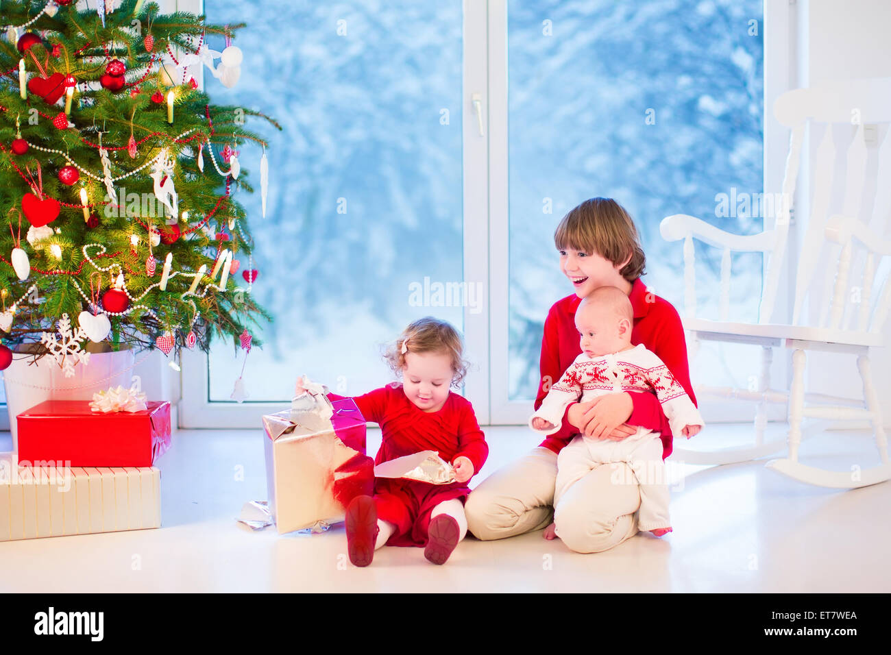 Three kids opening Christmas presents, enjoying Xmas morning in a ...