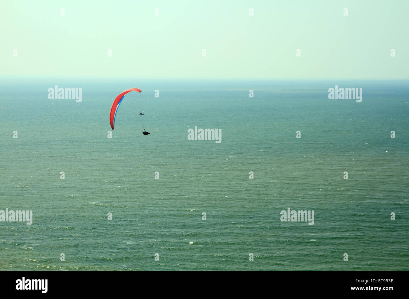 Red paraglider flying in blue sky over the ocean Stock Photo - Alamy