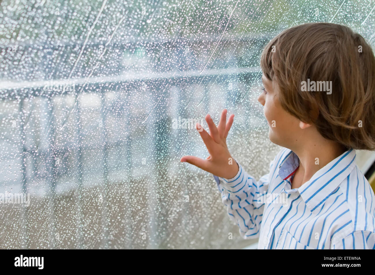 Smiling boy watching the rain outside at a window Stock Photo - Alamy