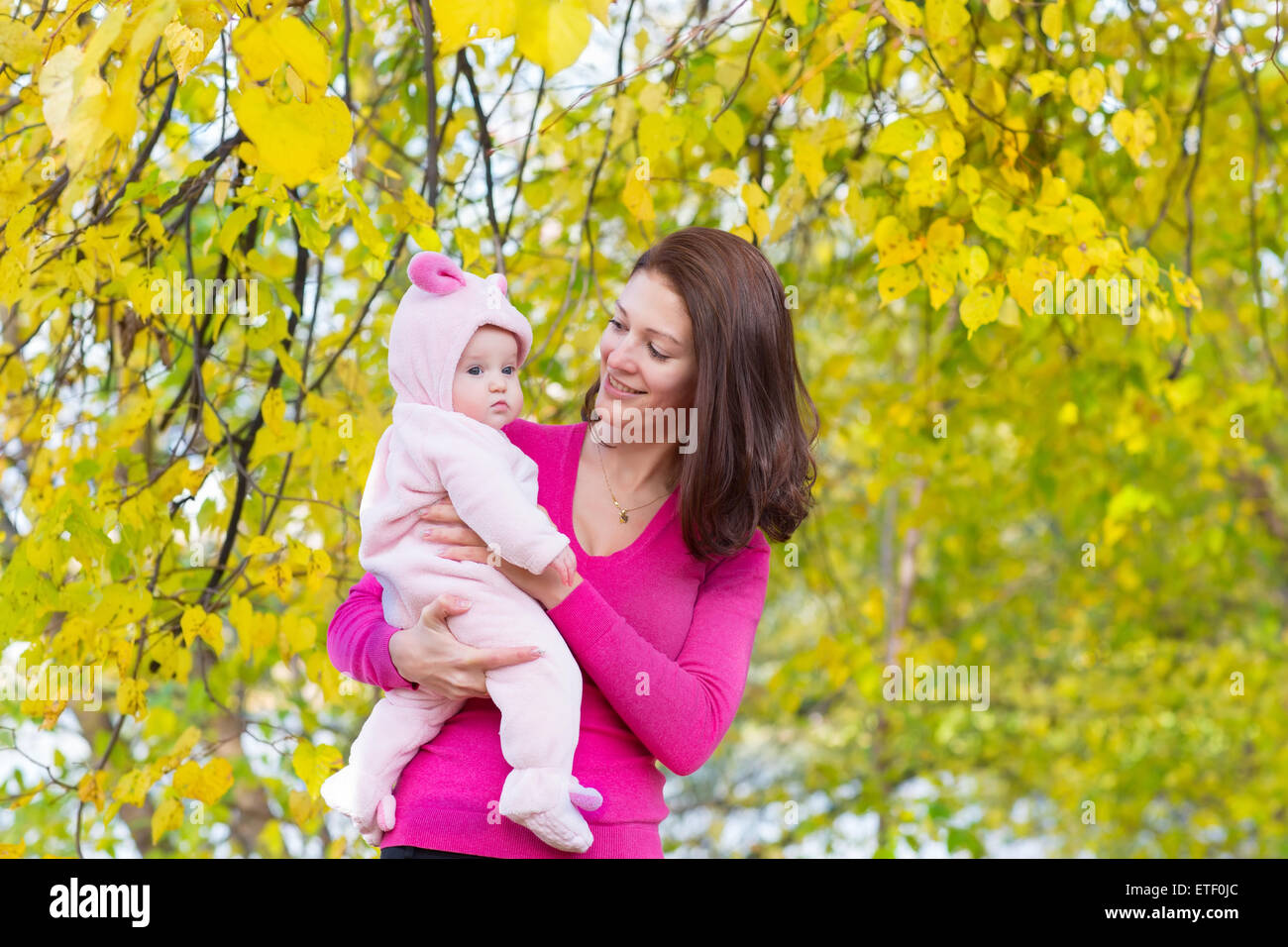Mother and baby daughter standing under a yellow tree on a sunny autumn ...
