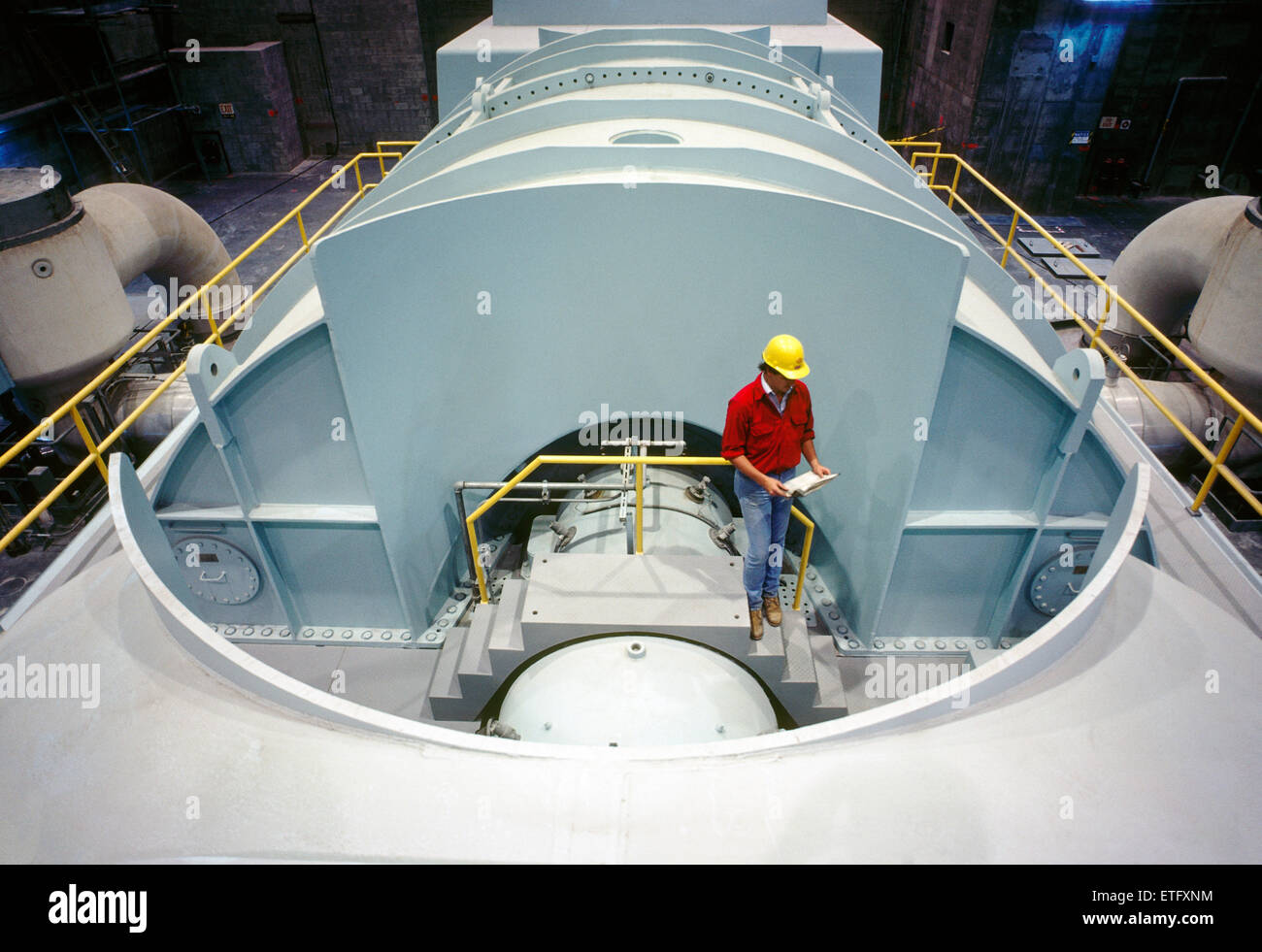 Male engineer inspecting drawings near a steam turbine, nuclear power ...