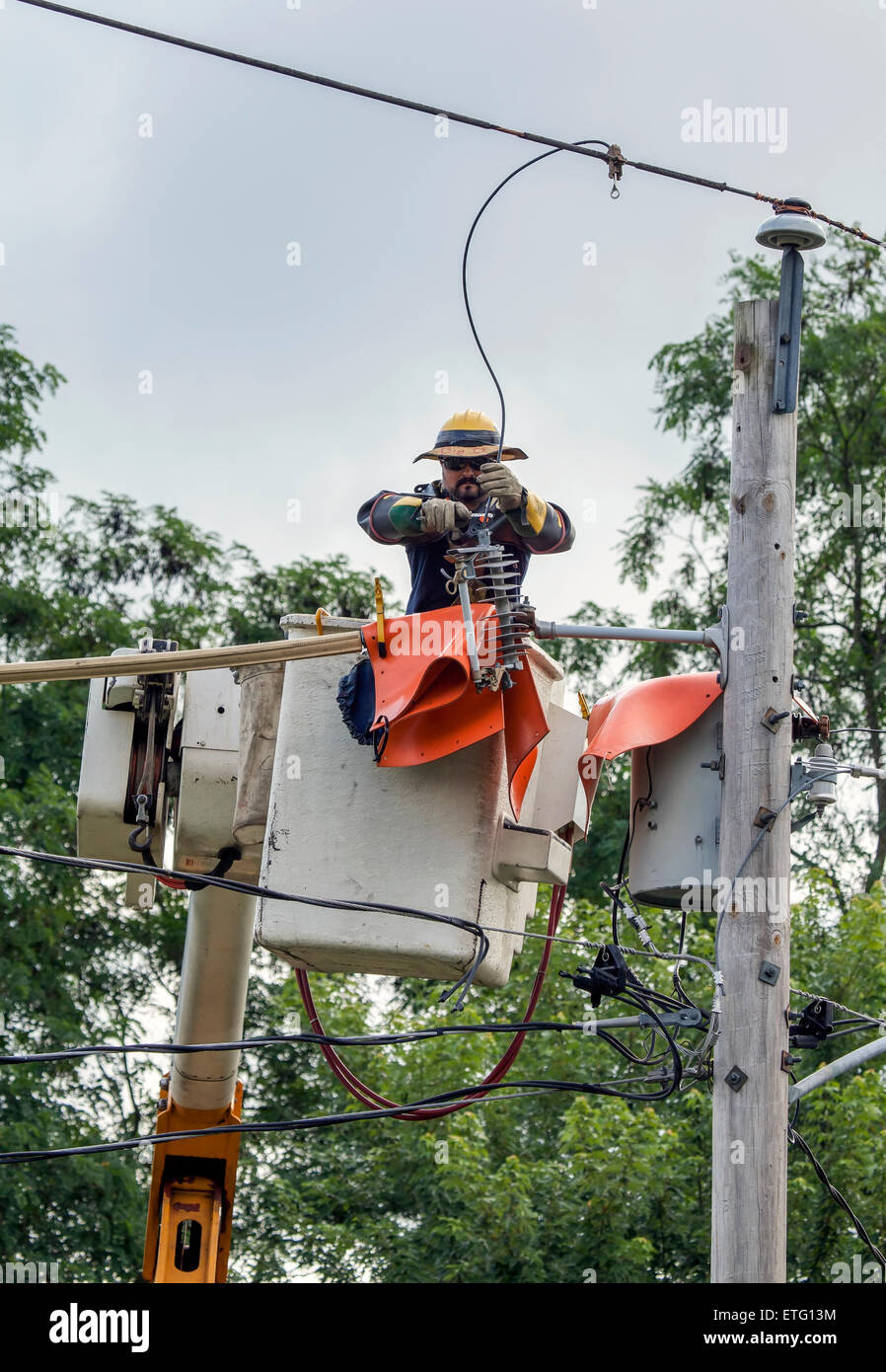 A telcom lineman fixes overhead power lines using a cherry picker ...