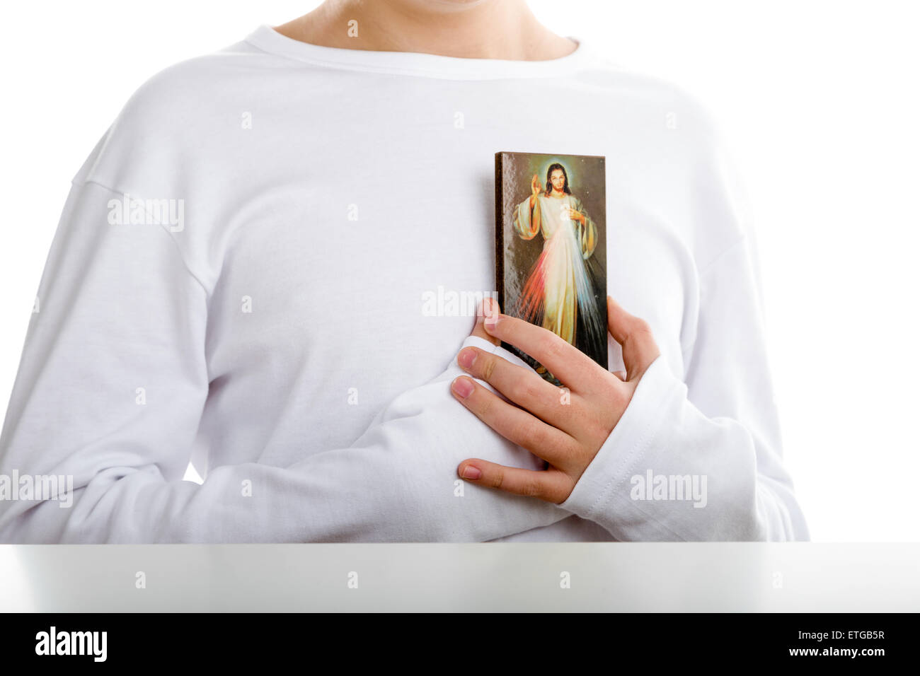 A Caucasian boy holds resting on his chest a picture of Merciful Jesus ...