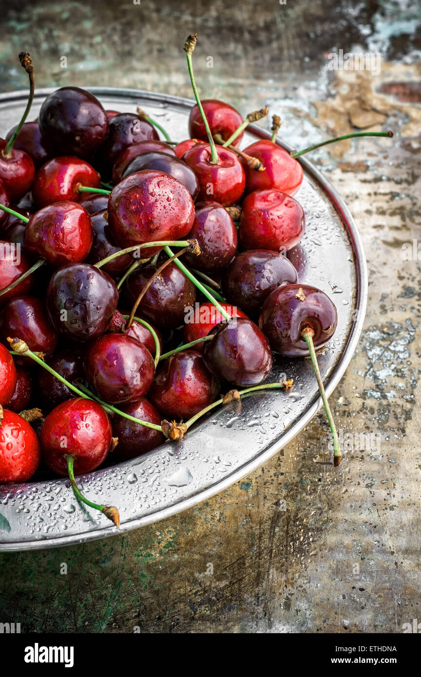 ripe large cherries in the iron bowl iron on the background in bright ...