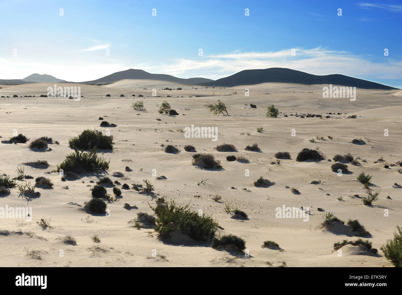 Two people walking on sand dunes with mountains and blue sky with some ...